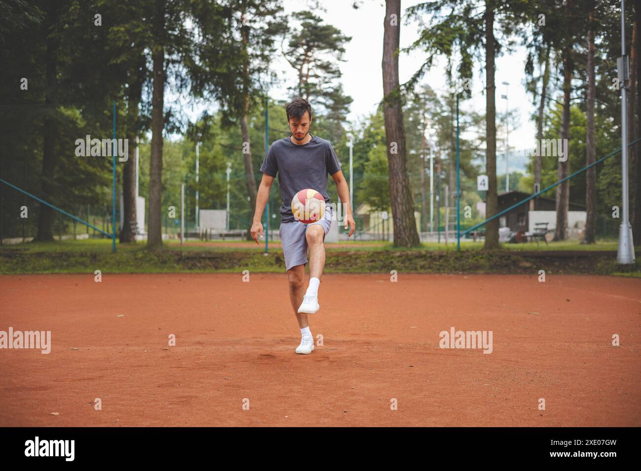 Soccer player in 20s plays with a balloon on a clay court. Amateur ...