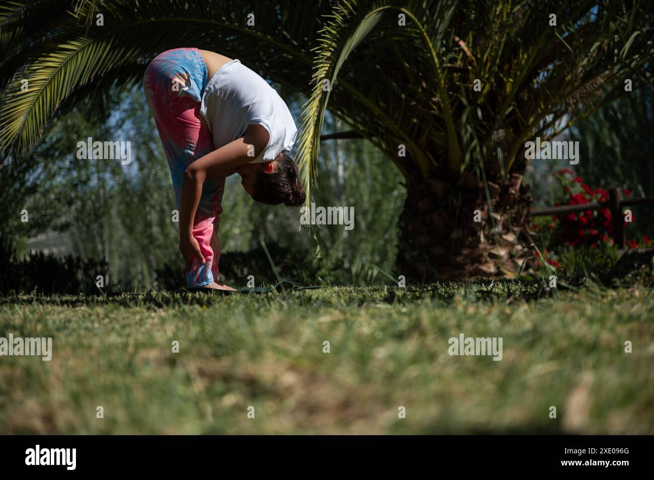 A woman practicing yoga in an outdoor garden setting, performing a ...