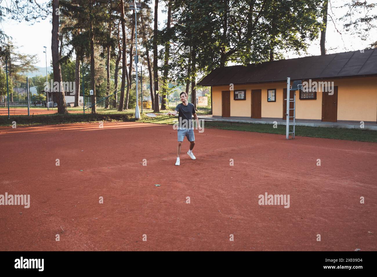 Black-haired athlete with a smile on his face plays badminton on a clay ...