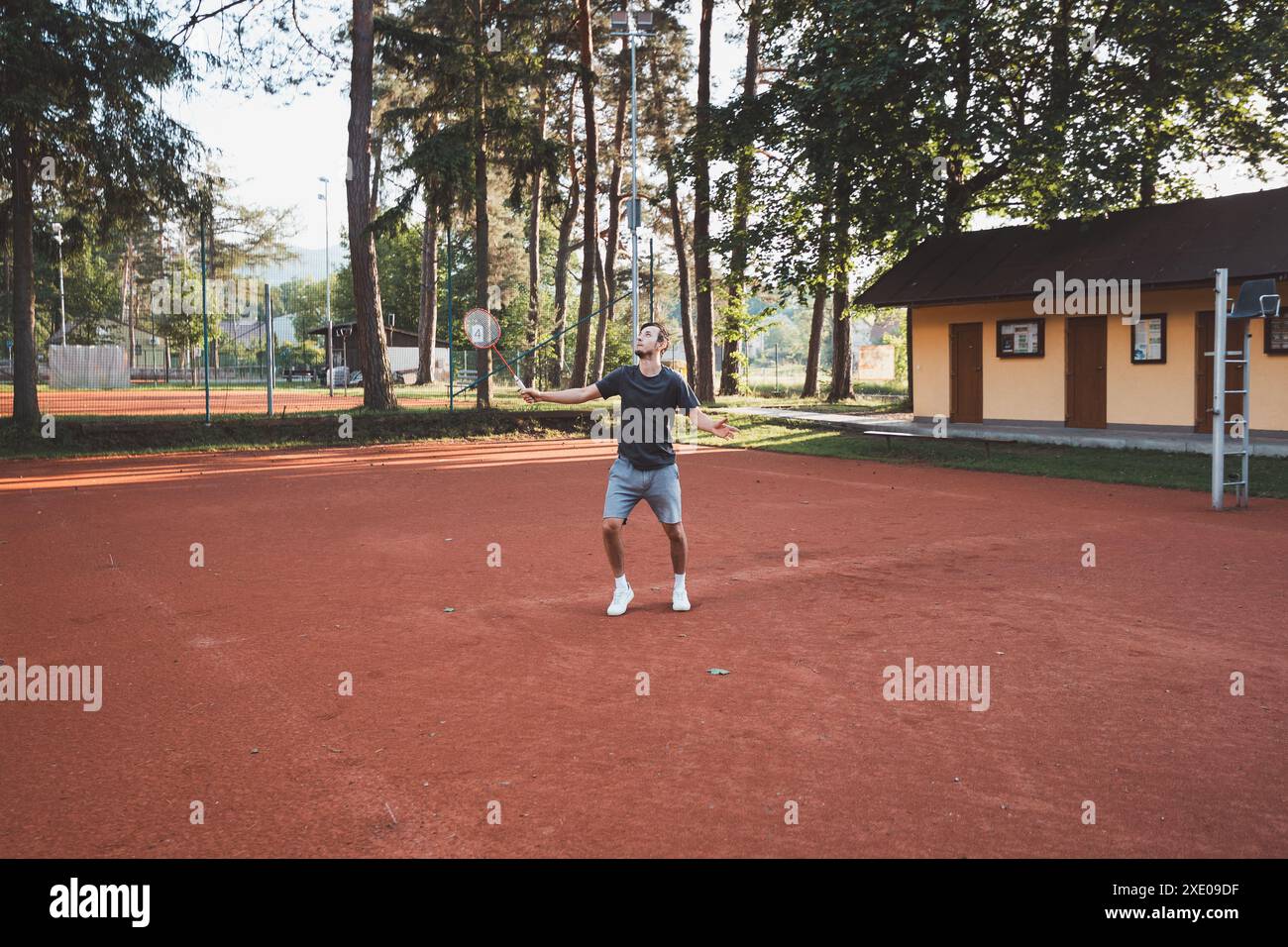 Black-haired athlete with a smile on his face plays badminton on a clay ...