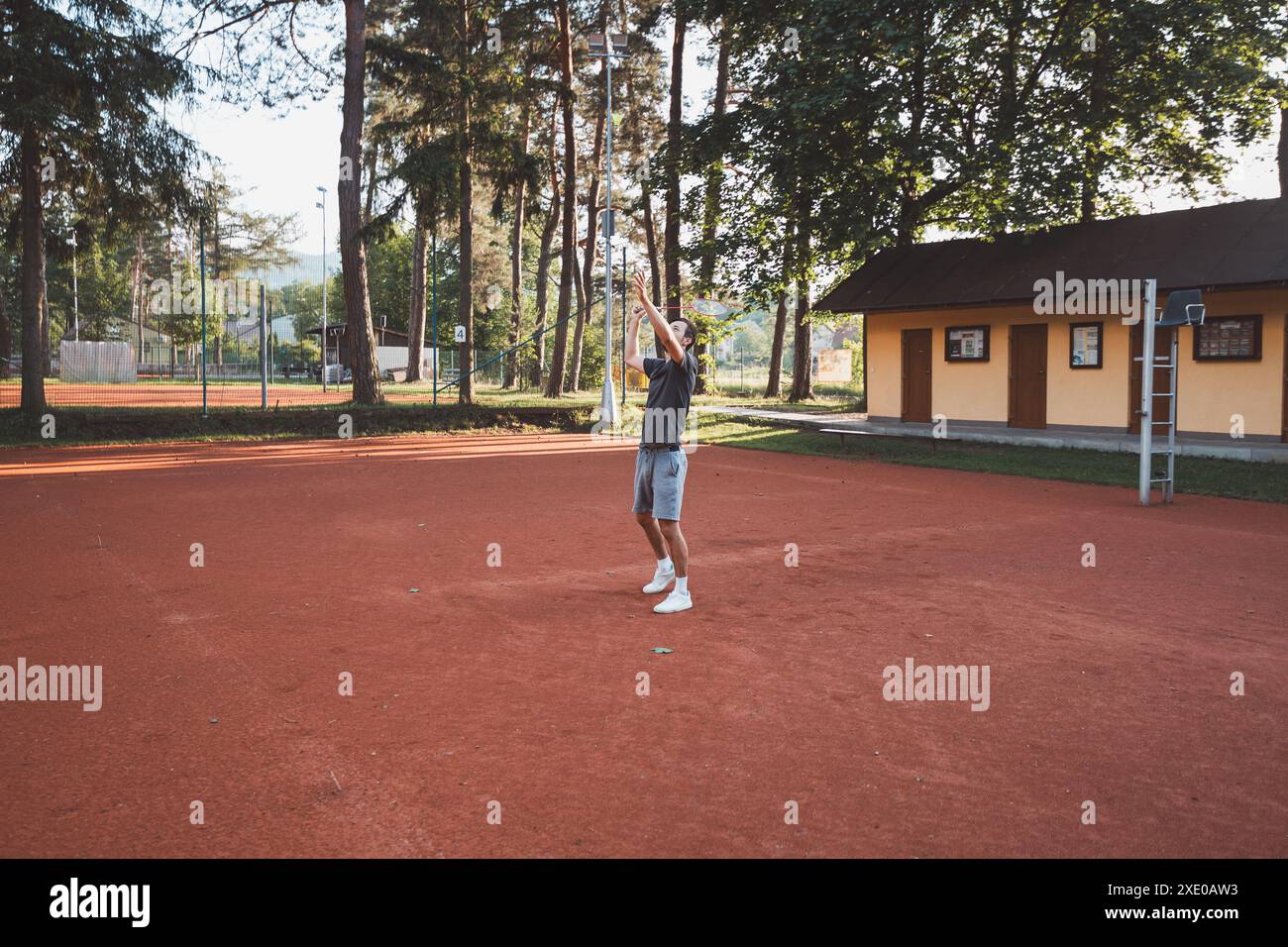 Black-haired athlete with a smile on his face plays badminton on a clay ...