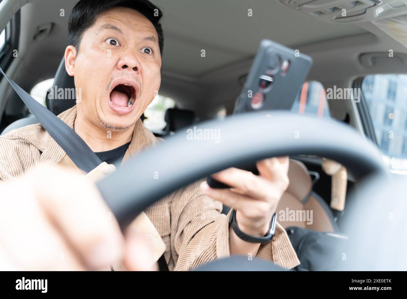 A man is driving a car and looking at his cell phone. He is yelling and ...