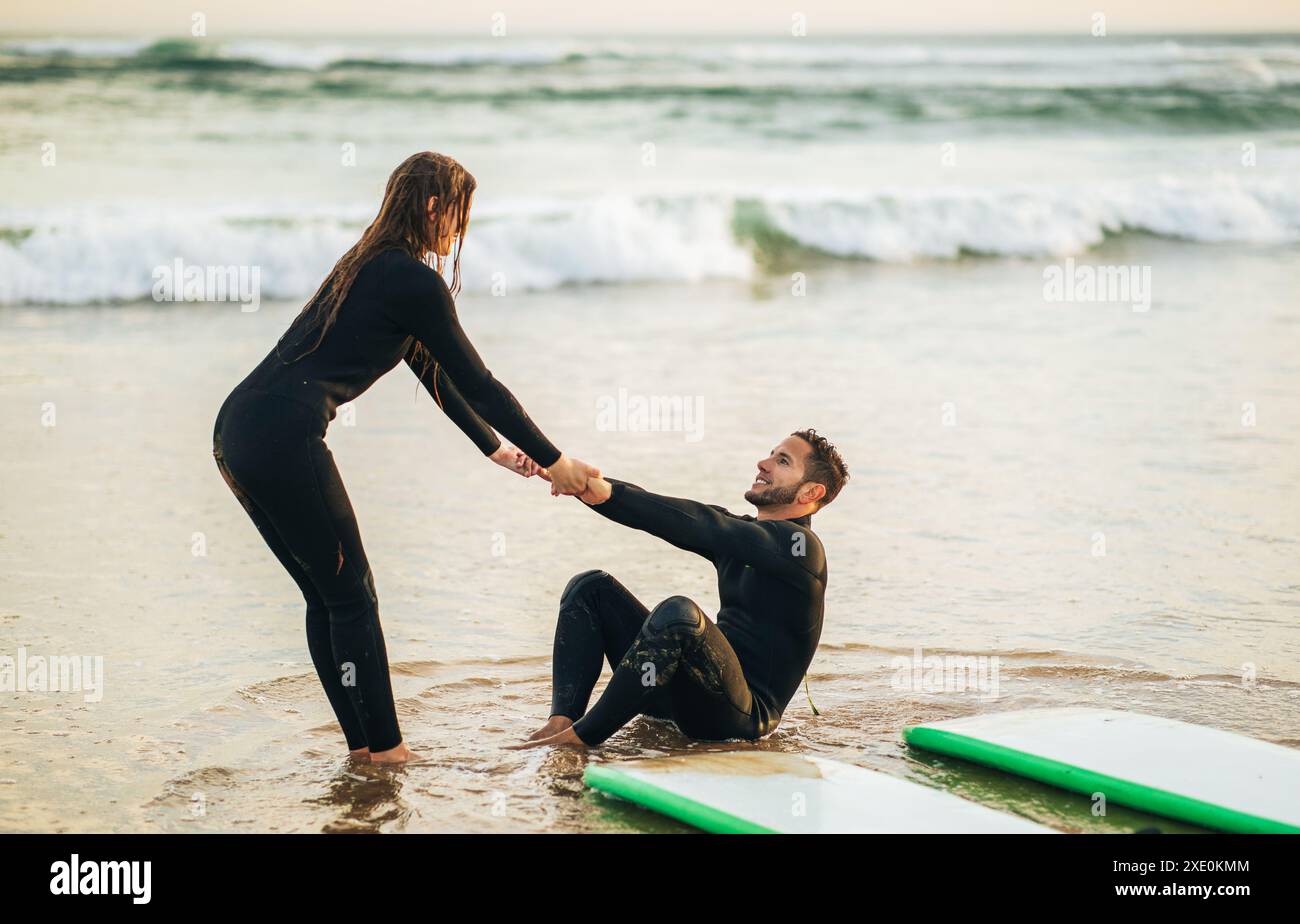 Woman Helping Man Up After Falling Off Surfboard on Beach Stock Photo ...
