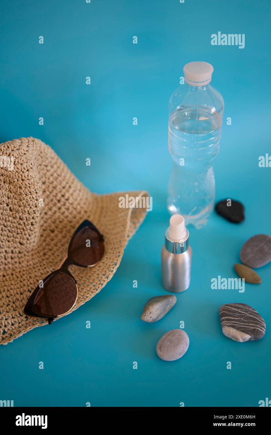 straw hat, sunglasses, bottle of water, sun spray, pebbles on a colored ...