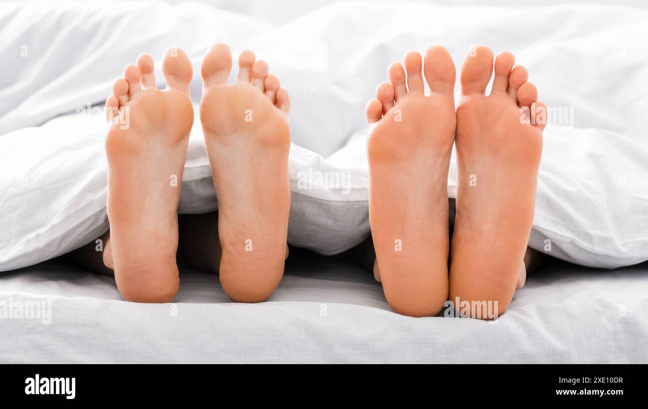 Two Pairs of Feet Under White Sheets in a Bed Stock Photo - Alamy