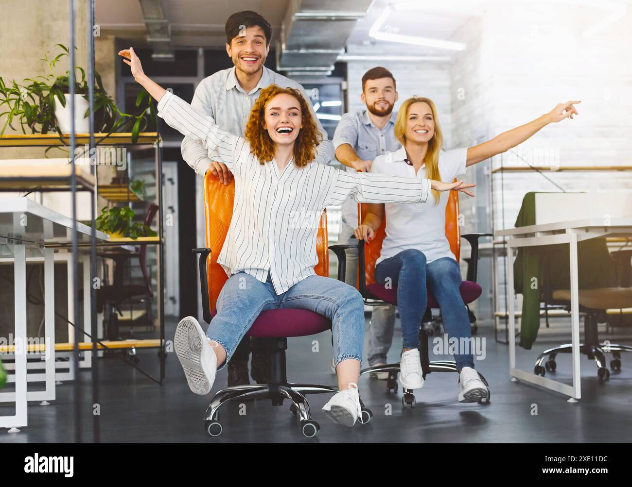 Happy colleagues having fun at workplace, making office chair race ...