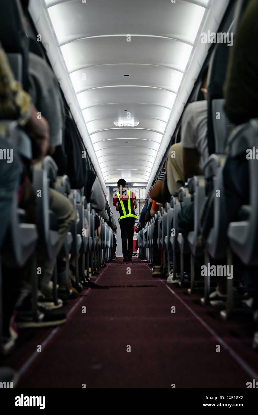 A crew in safety vest uniform performing checks in aisle of airplane ...