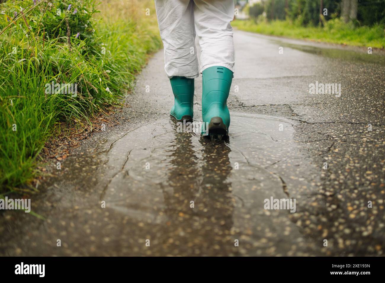 Woman wearing rain rubber boots walking running and jumping into puddle ...