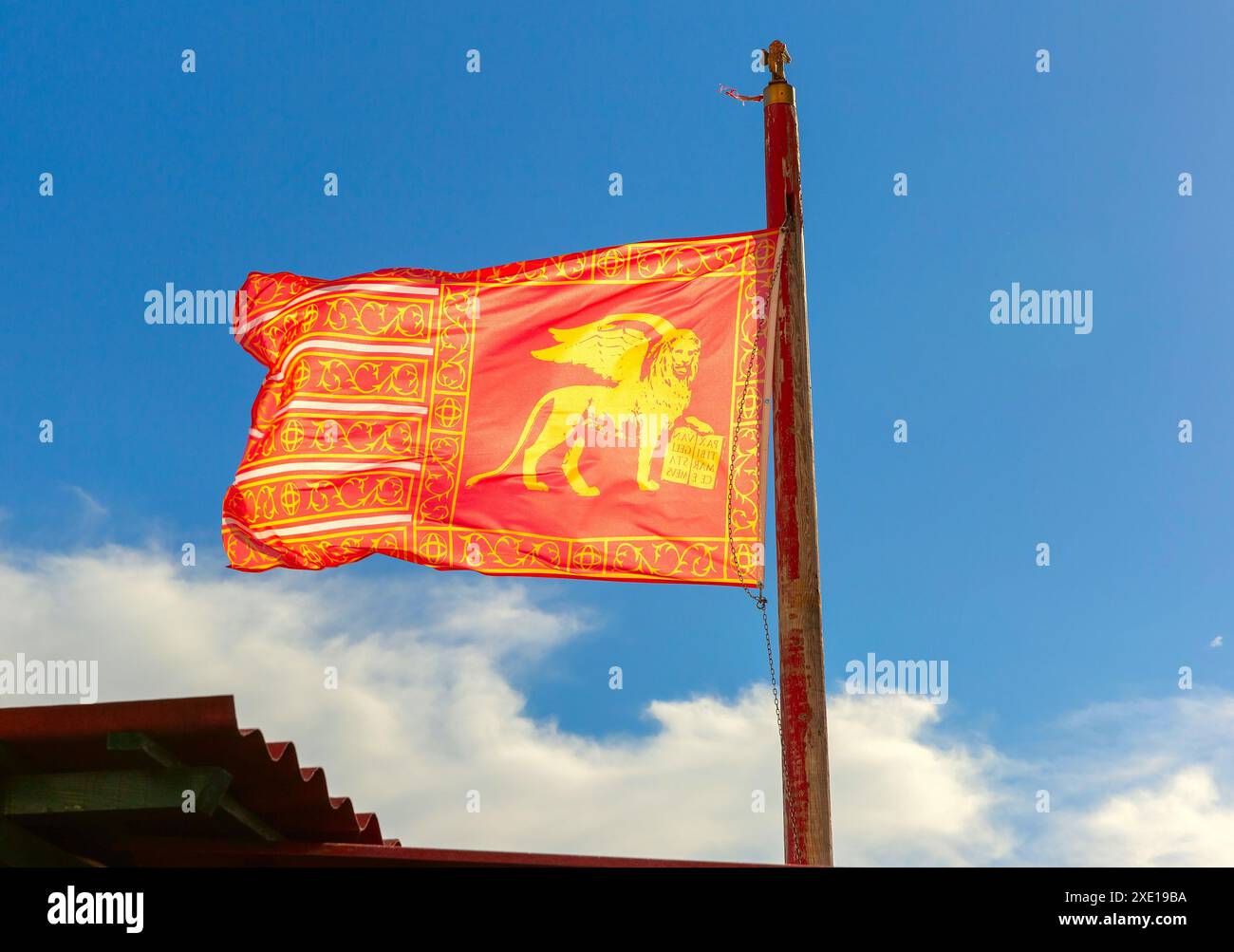 Golden winged lion on the red standard of St. Mark against the blue sky ...