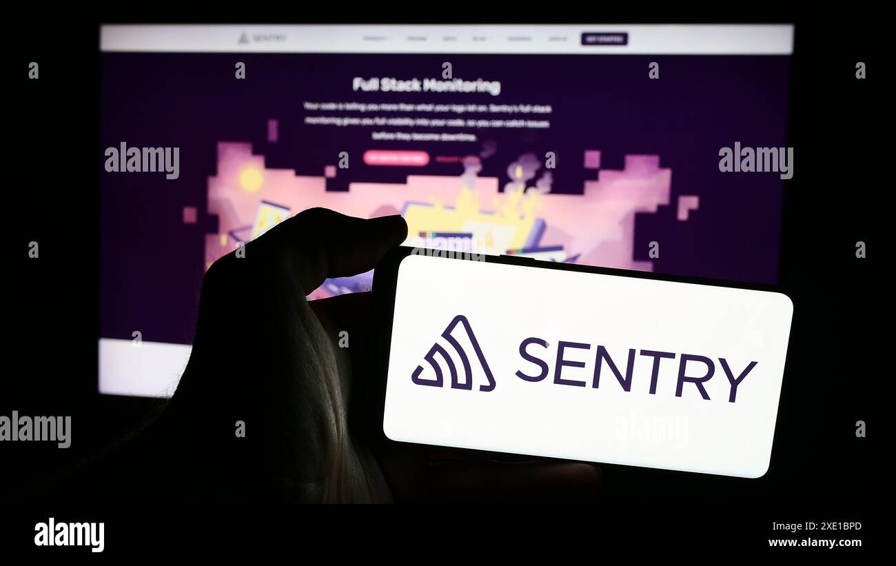 Person holding mobile phone with logo of American company Functional Software Inc. (Sentry) in ...