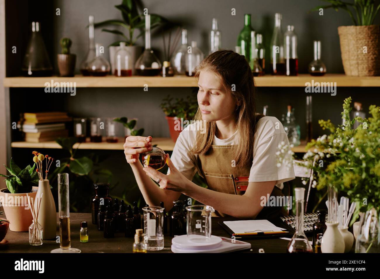 Young female perfumer admiring new samples of handmade perfume in home ...