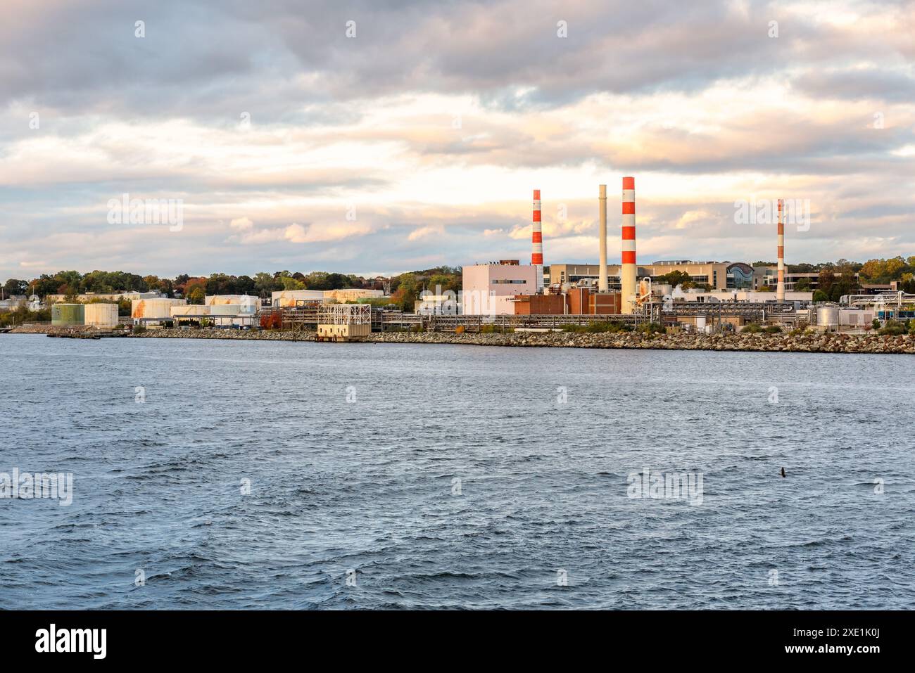 Riverside power plant and an oil terminal under cloudy sky at sunset ...