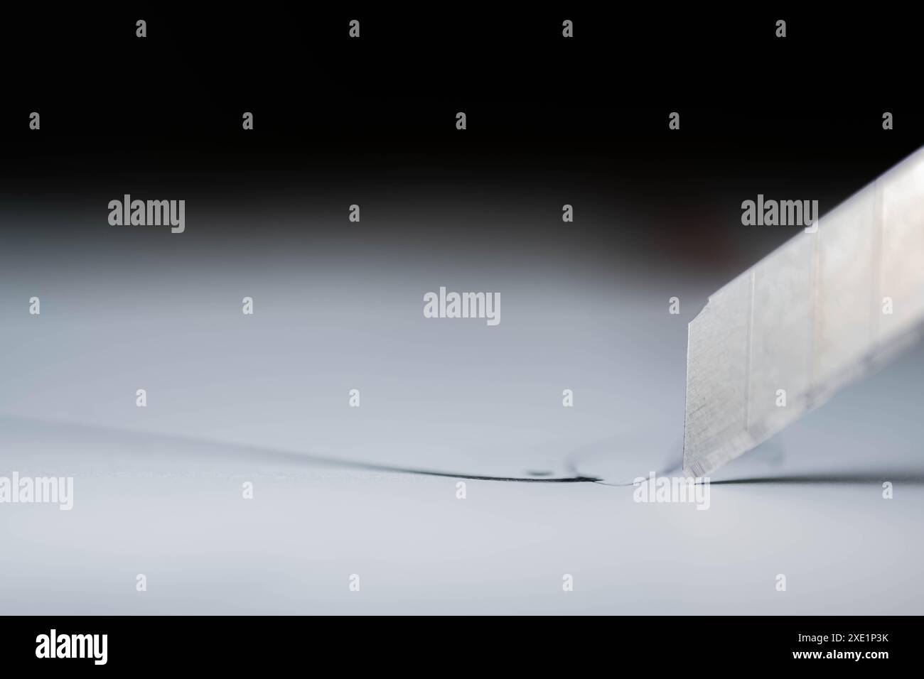 Close-up of a utility knife blade cutting through a sheet of paper ...
