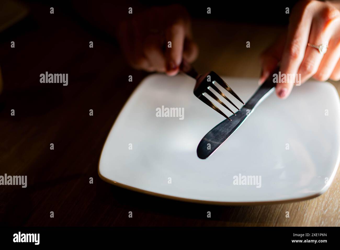 A person holding a fork and knife over an empty white plate, preparing ...