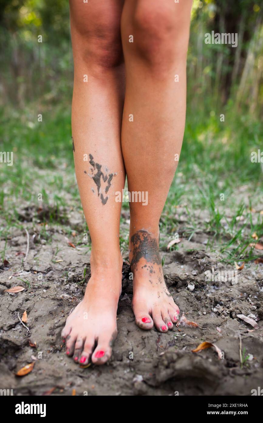 This image captures the lower legs and feet of a woman covered in mud ...