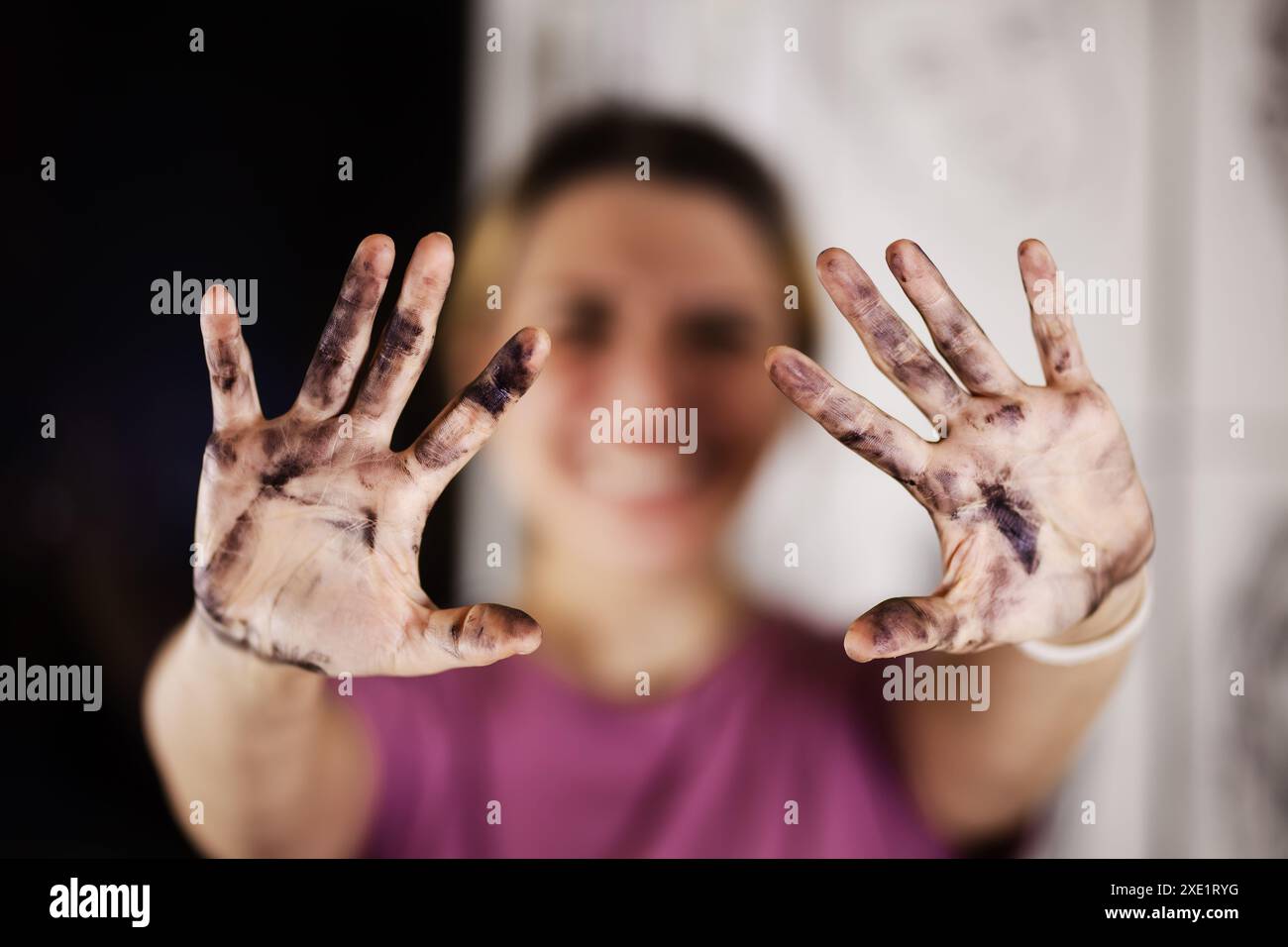 A female painter in a casual purple shirt displays her messy hands ...