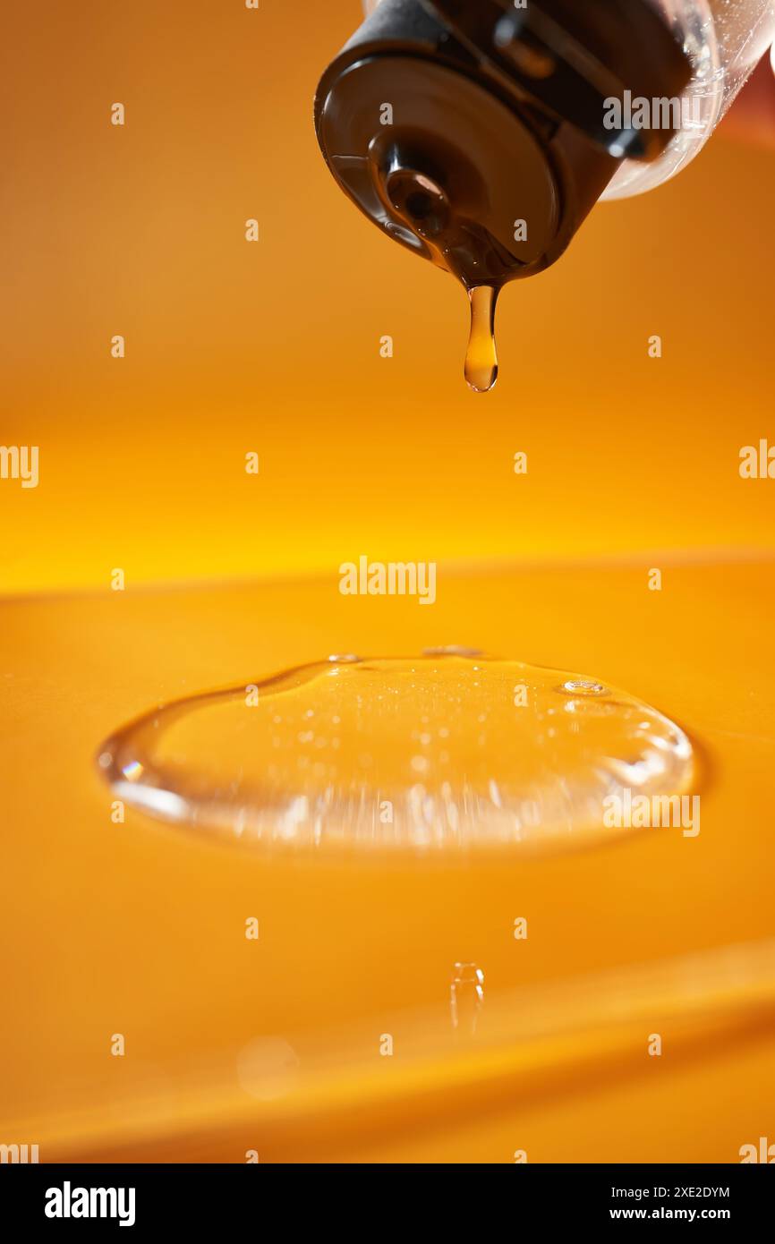 A drop of body gel or shampoo pouring from above on a yellow saturated ...