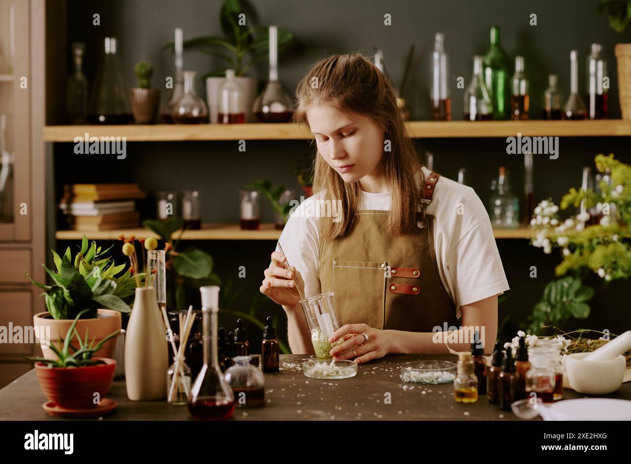 Female young perfumer mixing transparent liquid with dried wildflowers ...
