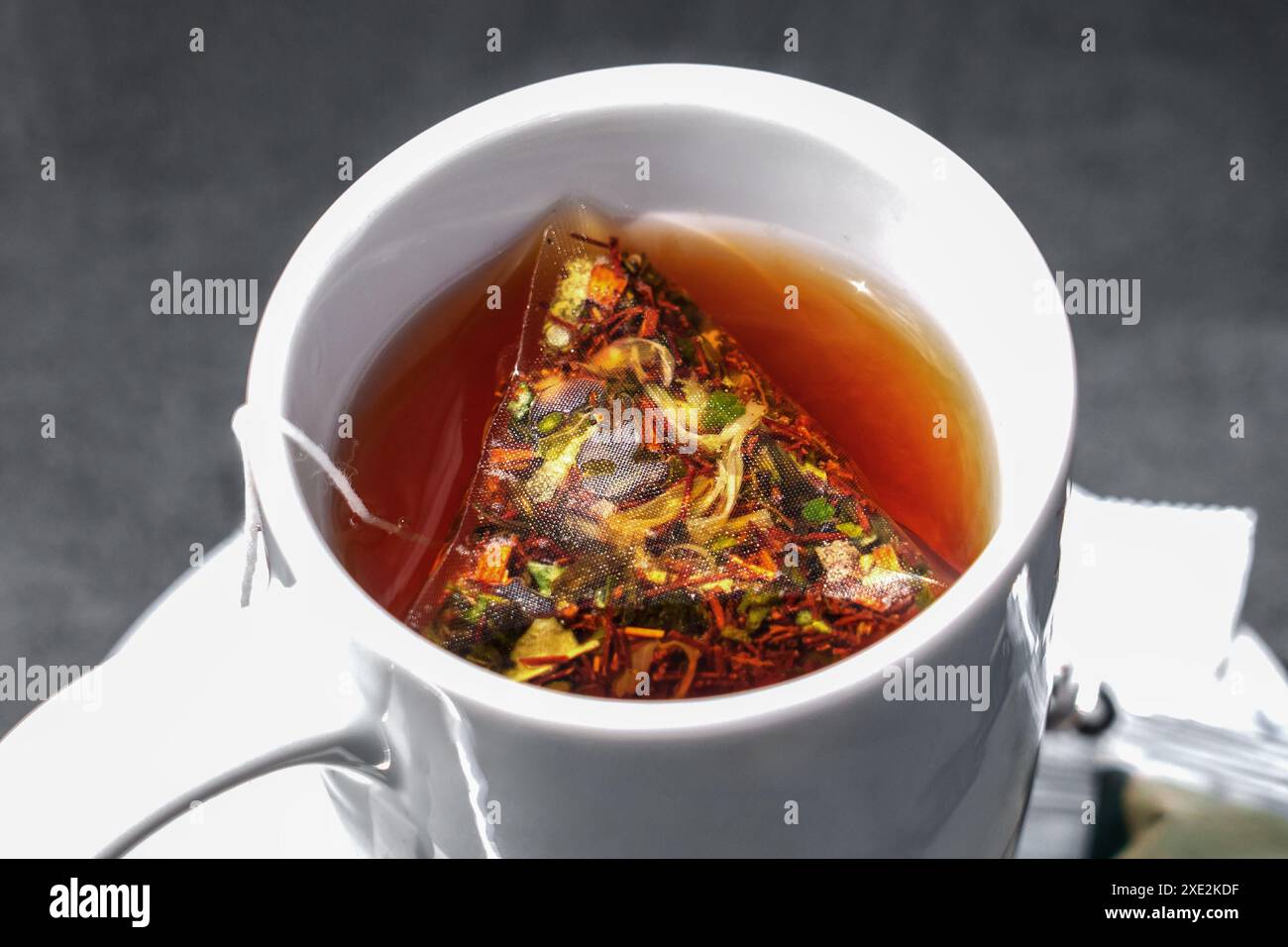 White mug with warm reddish-brown tea with a triangular teabag steeped ...
