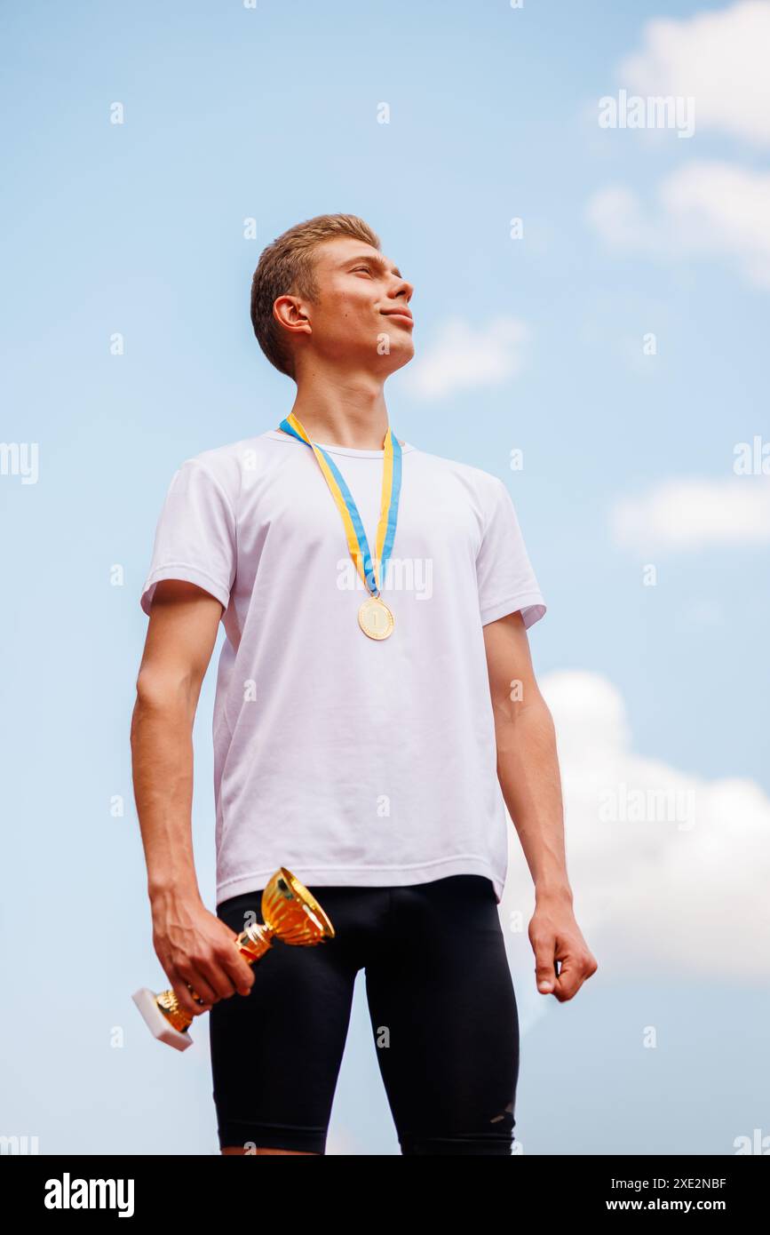 A young male athlete is holding a trophy and wearing a gold medal under ...