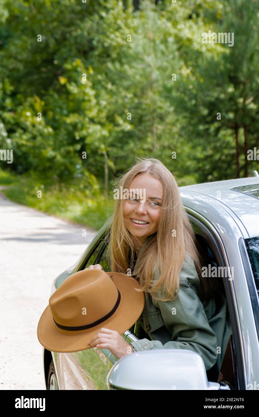 Blonde woman in hat sticking head out of windshield car. Young tourist ...