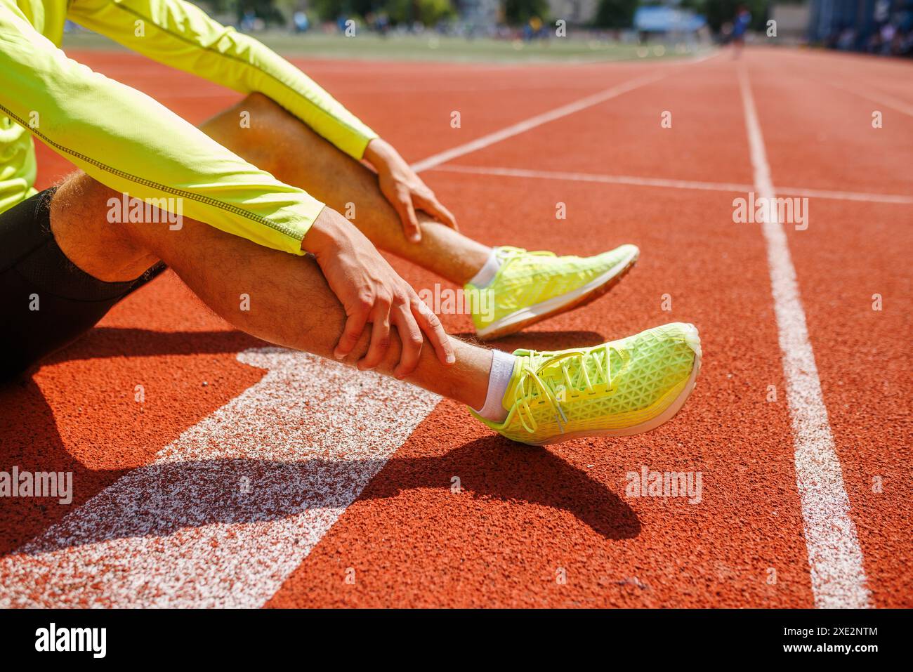 An athlete holds his legs before running while sitting in the stadium ...
