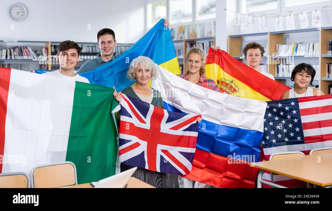 Portrait of positive teenagers and female teacher with flags of ...