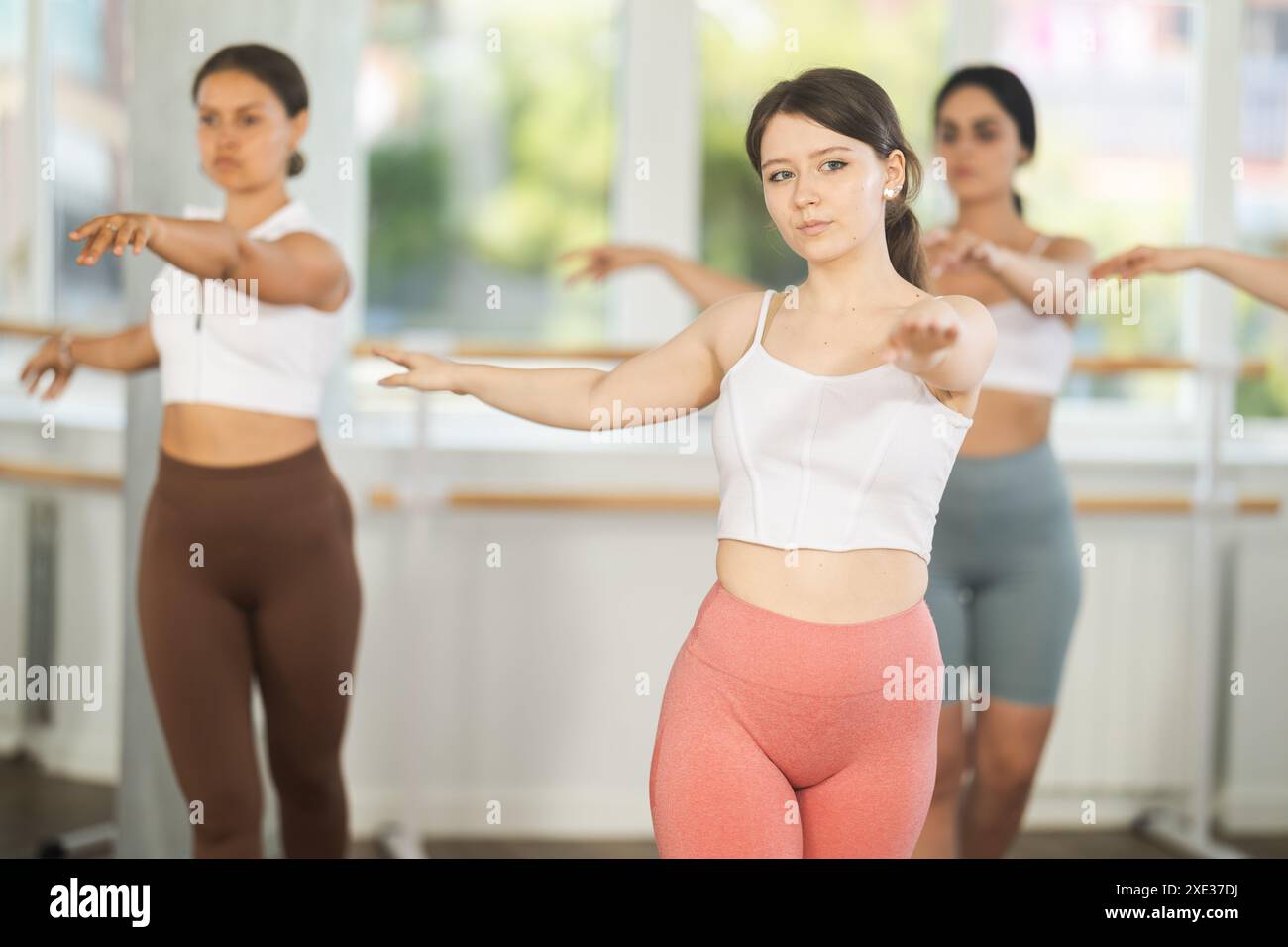 Cheerful slim active girl training various ballet poses during group ...