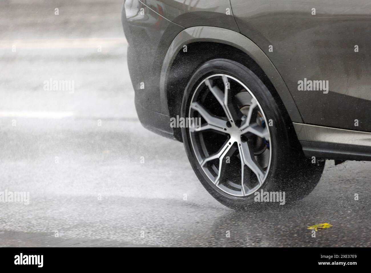 Rain water splashing flows from wheels of grey car that moving fast on ...