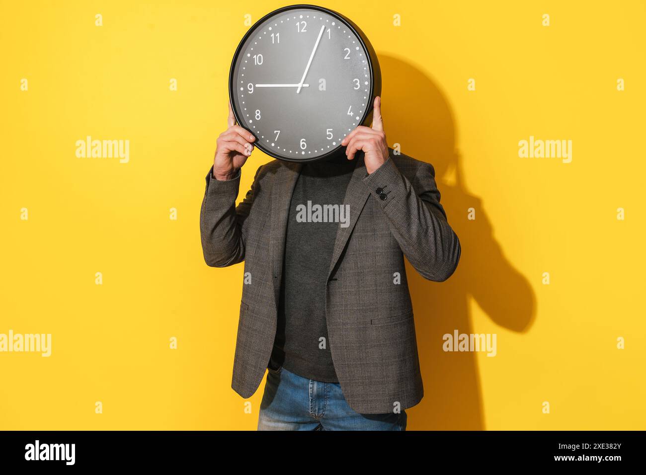 Man covering his face with big clock on yellow background Stock Photo ...