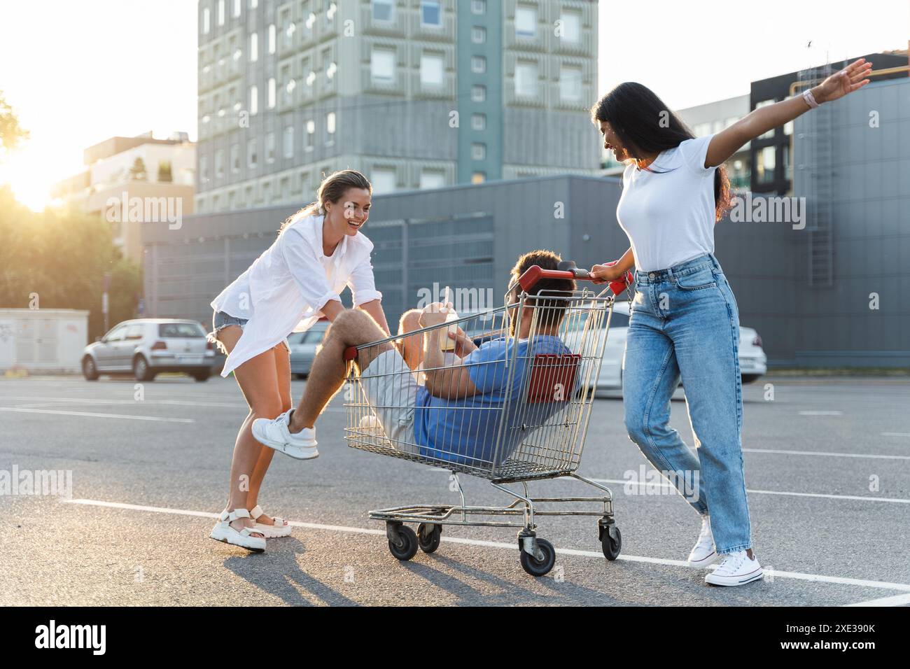 Three diverse friends having fun and riding shopping cart on parking ...