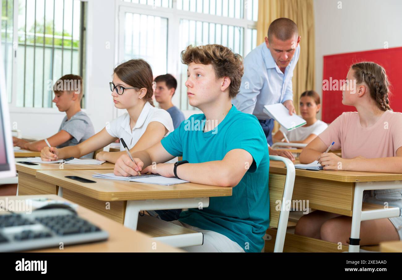 Teen boys and girls sitting at desk in classroom full of pupils during ...