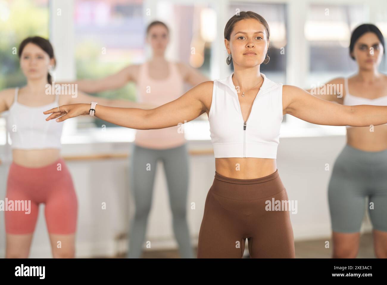 Cheerful slim active girl training various ballet poses during group ...