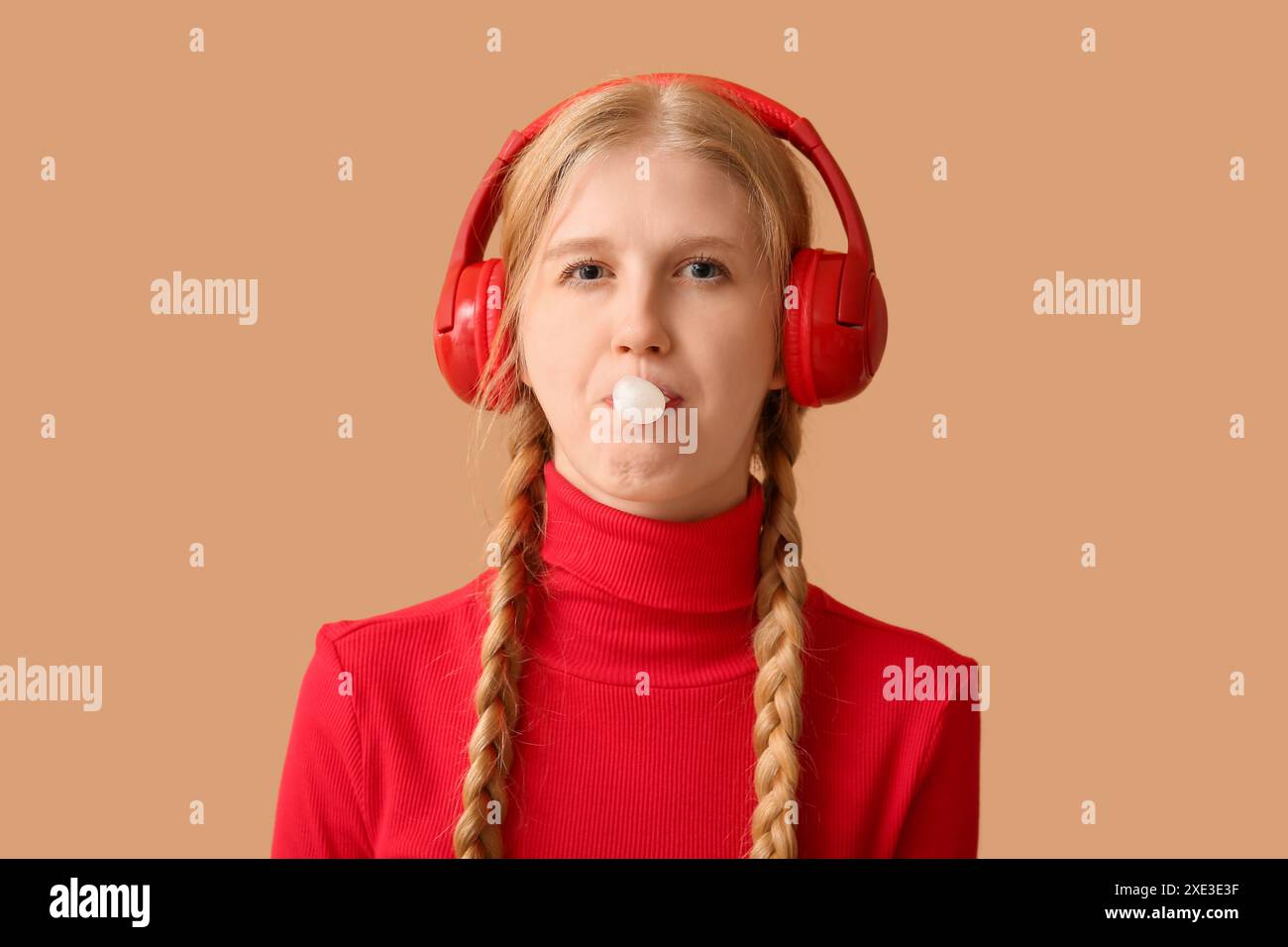Teenage girl in headphones chewing gum on beige background Stock Photo ...