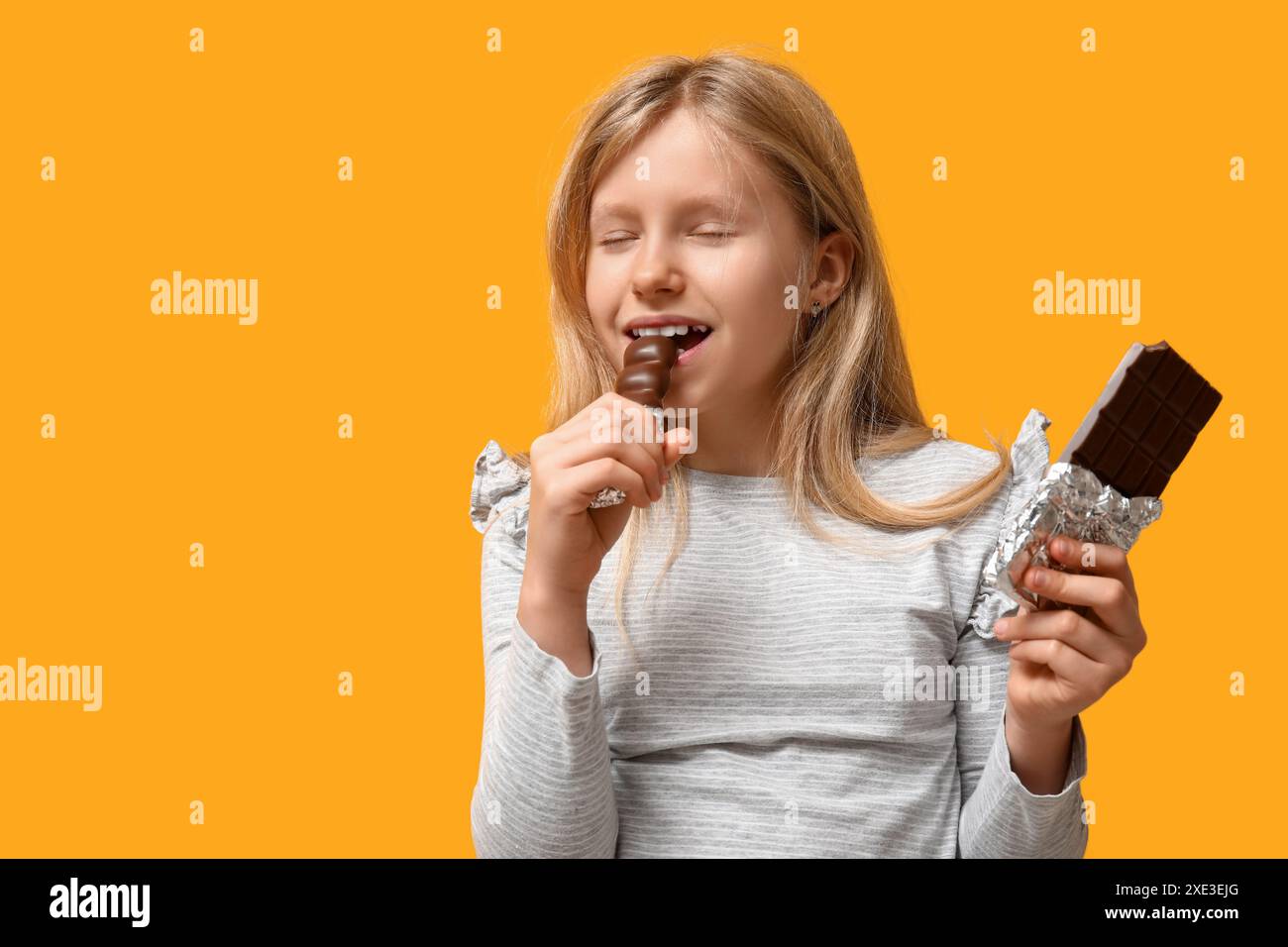 Cute little girl eating sweet chocolate on yellow background Stock ...