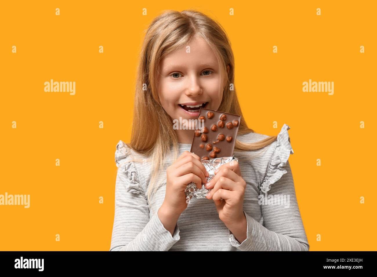 Cute little girl eating sweet chocolate bar on yellow background Stock ...