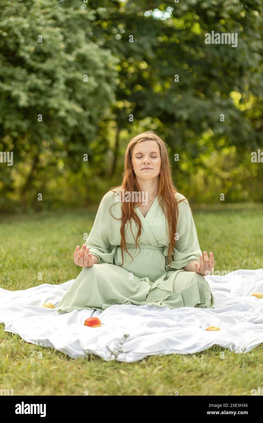 White pretty pregnant woman meditates in park, sits on blanket, stress ...