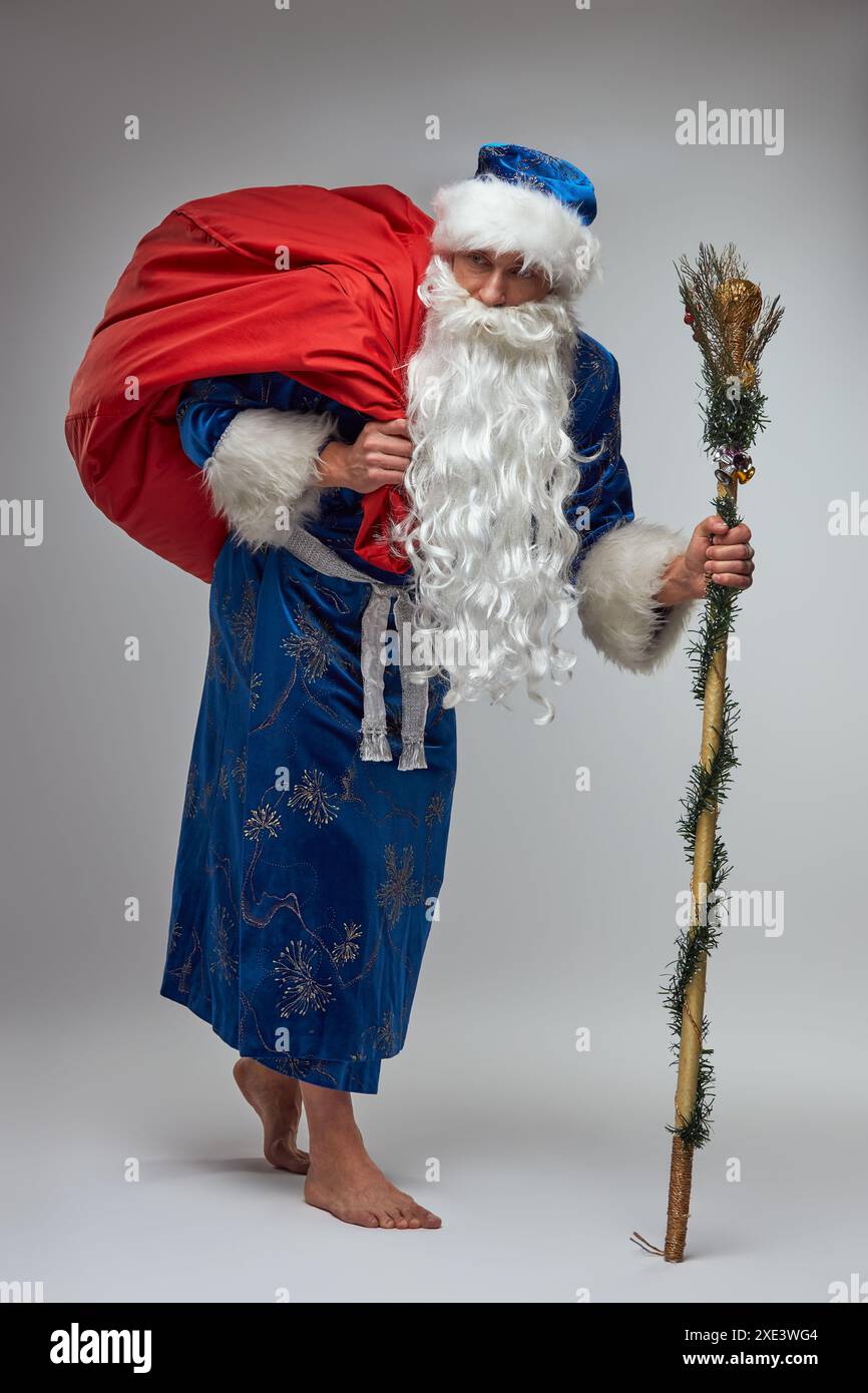 Barefoot Father Frost with staff carrying a bag of presents on his back ...