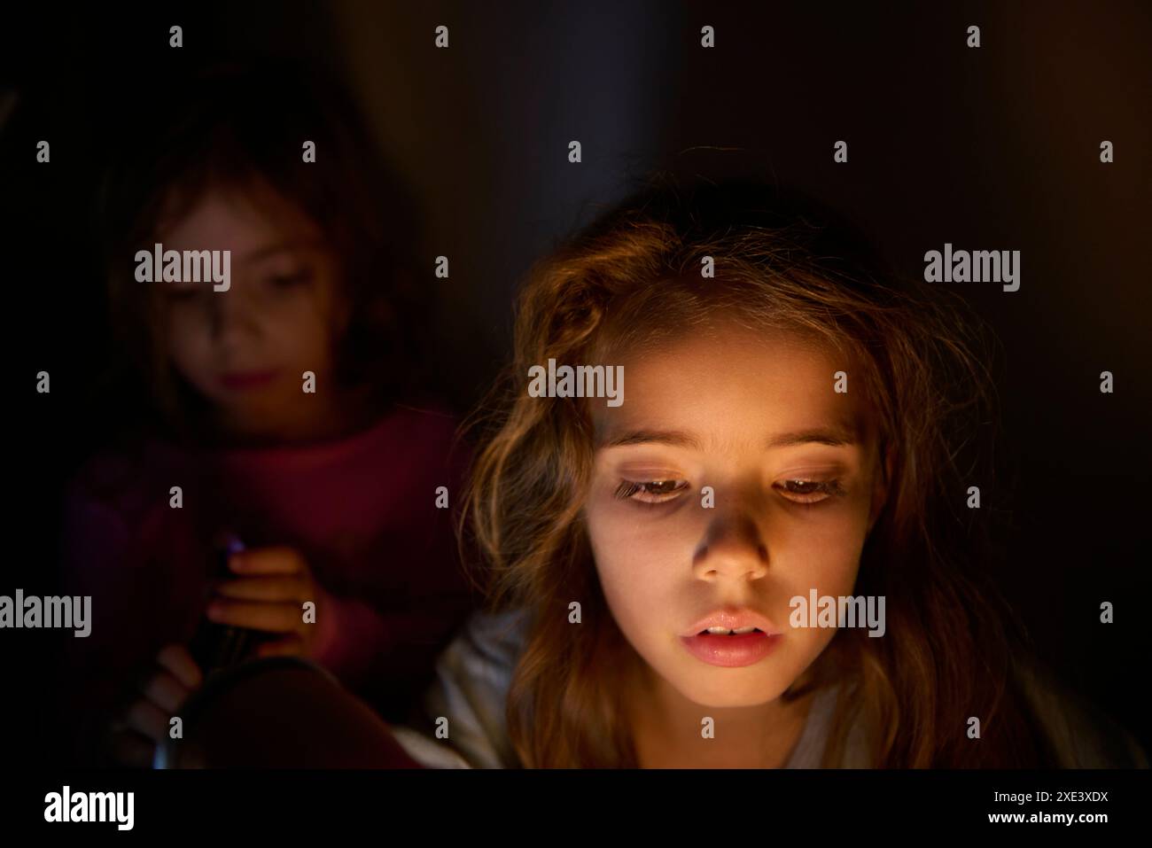 Girls are playing in a dimly lit room. The older one is looking down ...