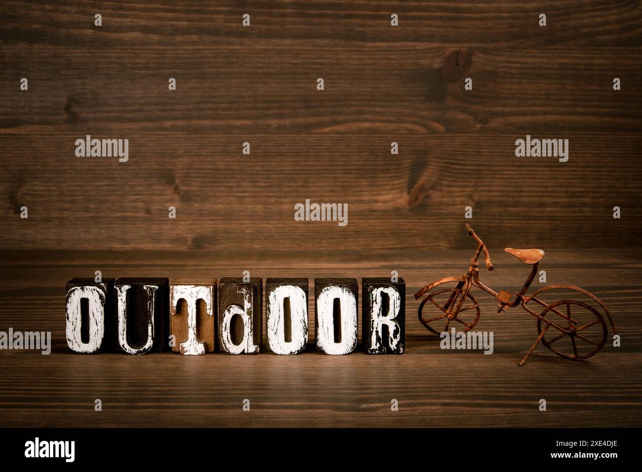 OUTDOOR. Word from alphabet blocks and rusty miniature bicycle on wood ...