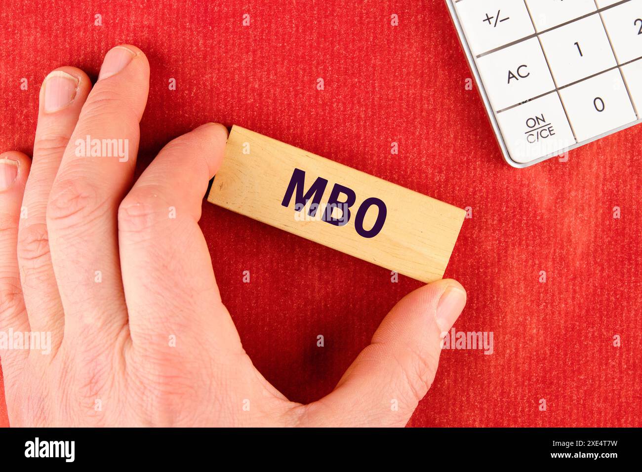 Management by Objectives MBO written on wooden blocks with a hand, part of a calculator on a red ...