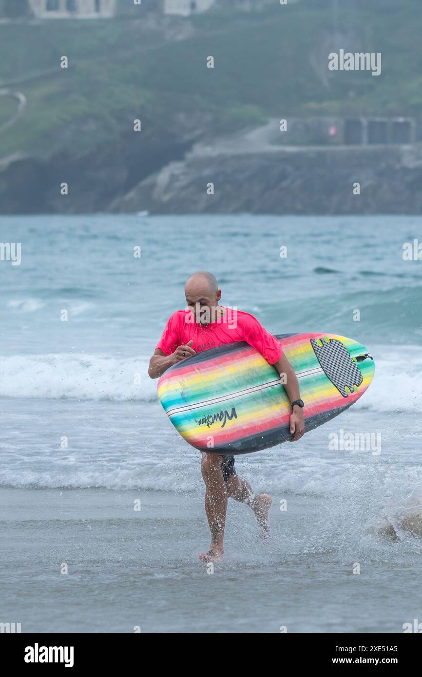 A surfer carrying his surfboard running out of the sea after competing ...