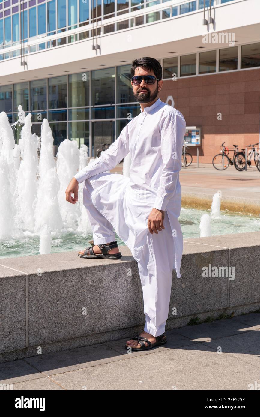 A Pakistani man with a dark beard in national white clothes stands near ...