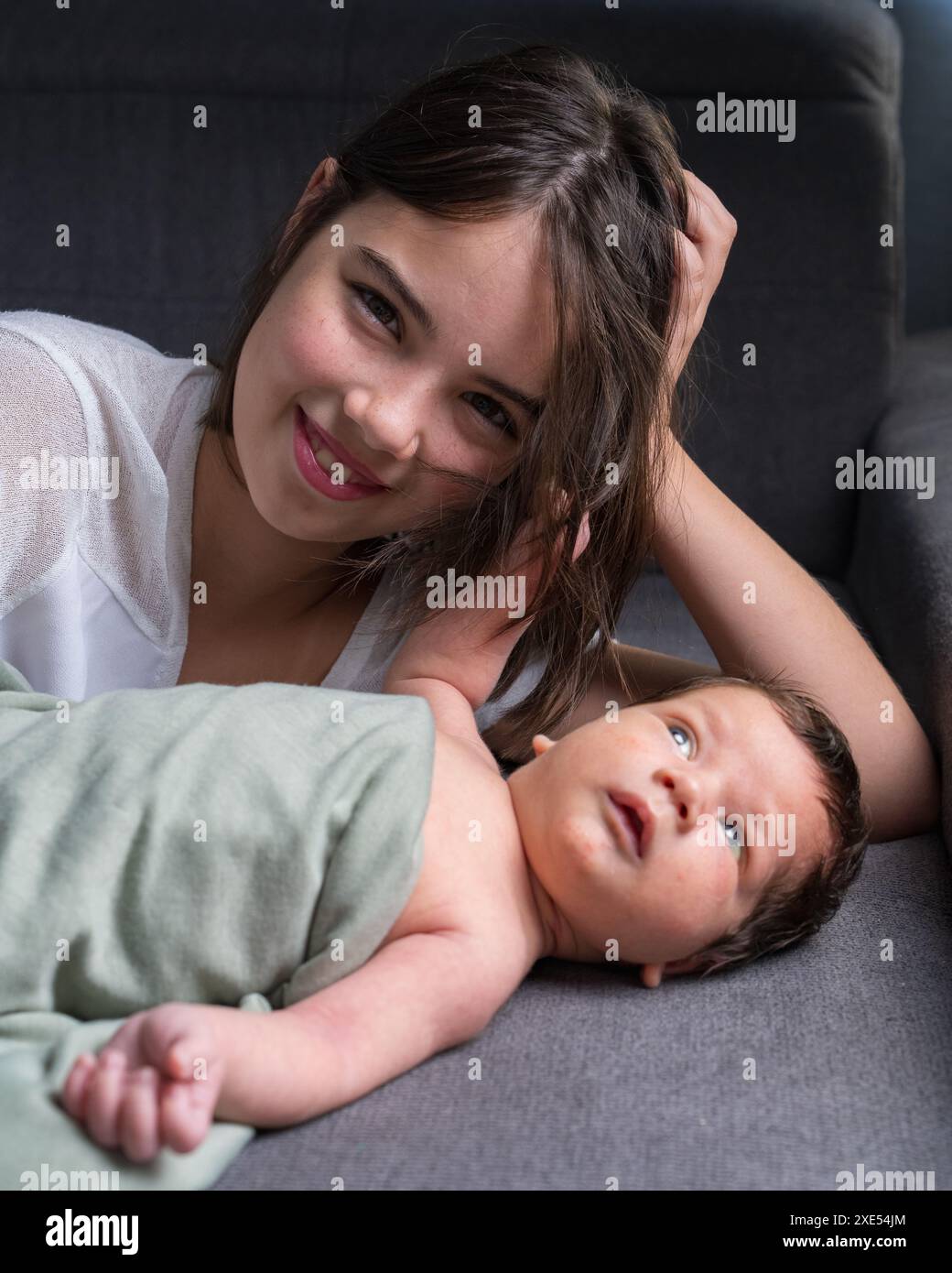 An older sister and her newborn little brother are lying on the sofa ...