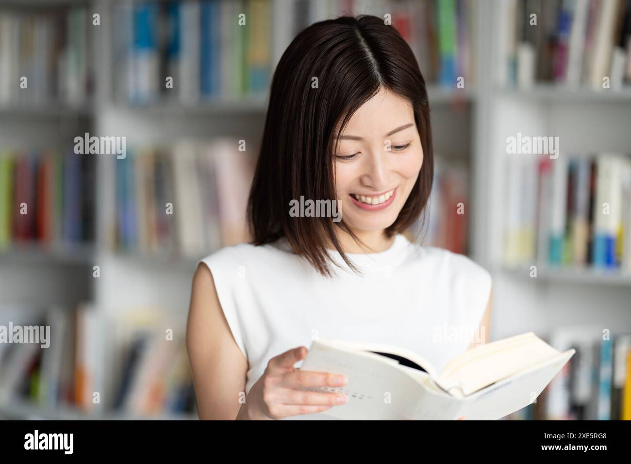 Woman laughing while reading a book in front of a bookshelf Stock Photo ...