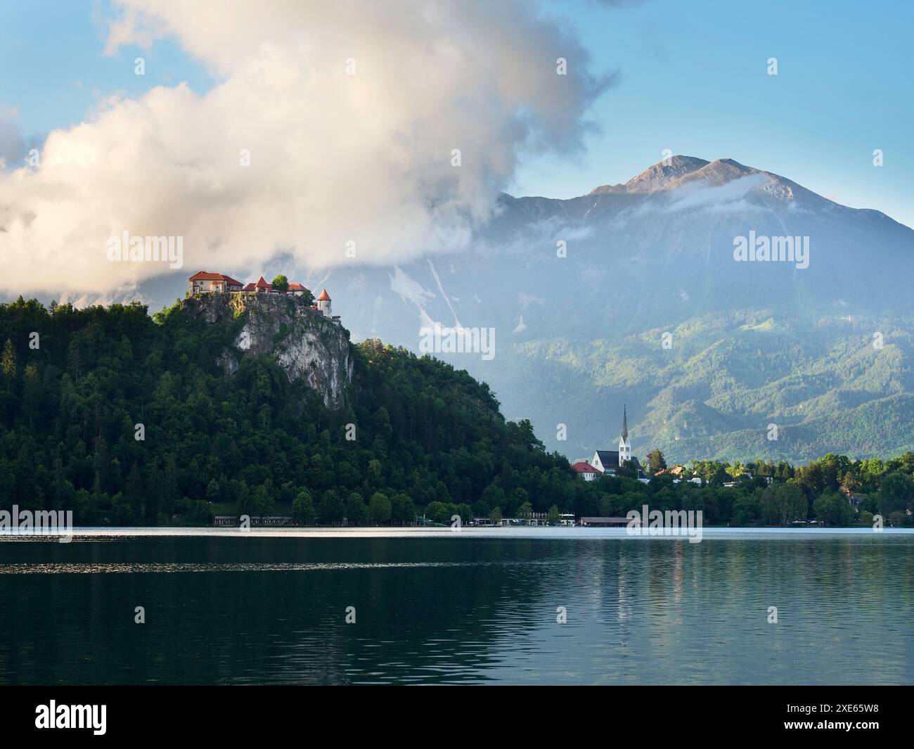 Sunlit clouds above Bled Castle looming over Bled Village on the shore ...