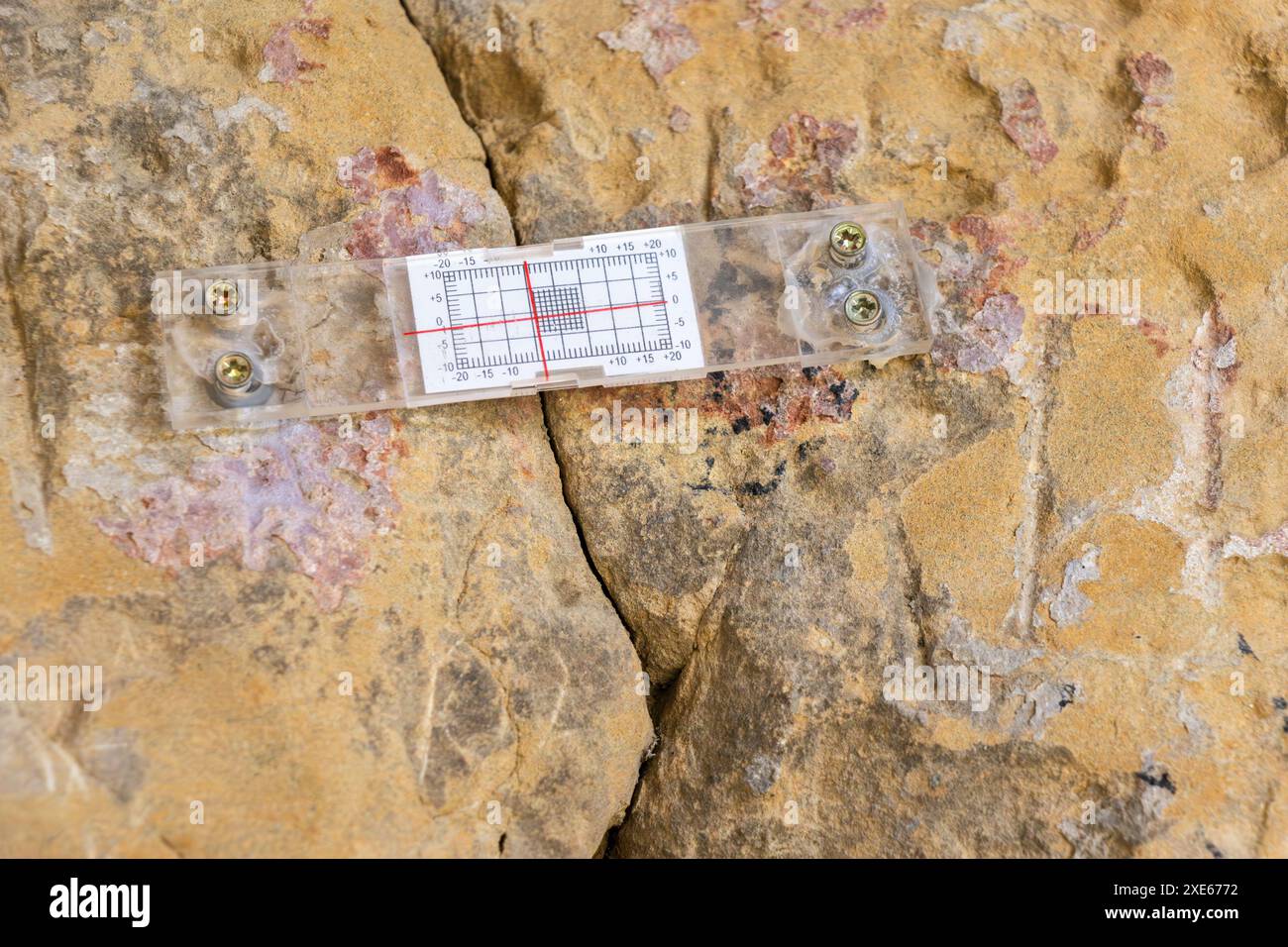 A close-up view of a transparent crack monitor attached to a rock ...