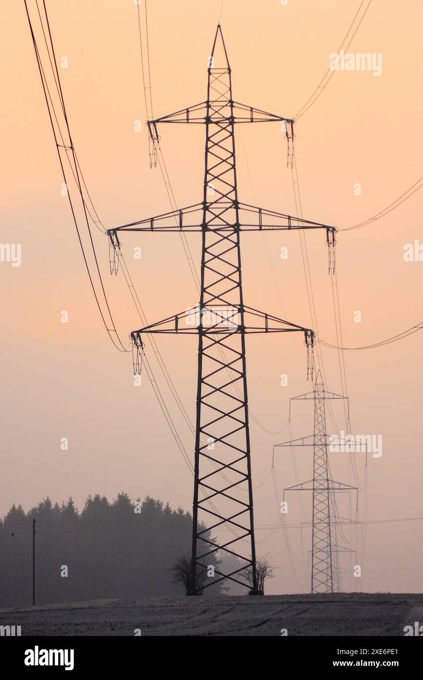 Setting sun behind silhouettes of electricity pylons and power lines ...