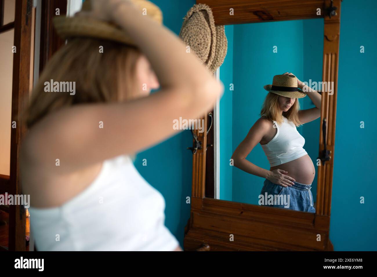 Pregnant Woman In Hat Smiling At Her Reflection In A Mirror Blue Wall