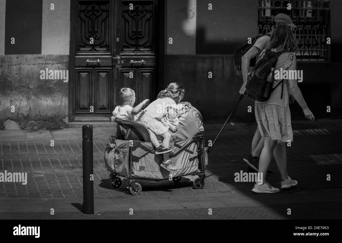 Family with parent travellers pulling children on a trolley through the streets of a European ...